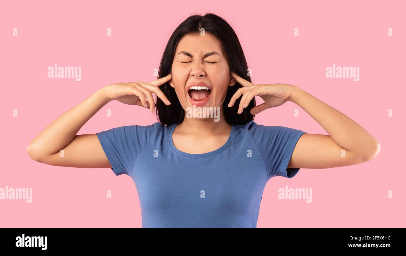 Angry asian woman plugging her ears with fingers and screaming Stock ...