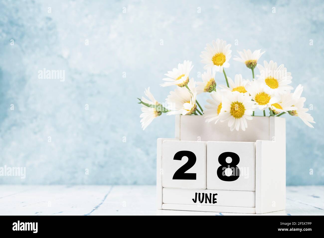 White cube calendar for June decorated with daisy flowers over blue ...