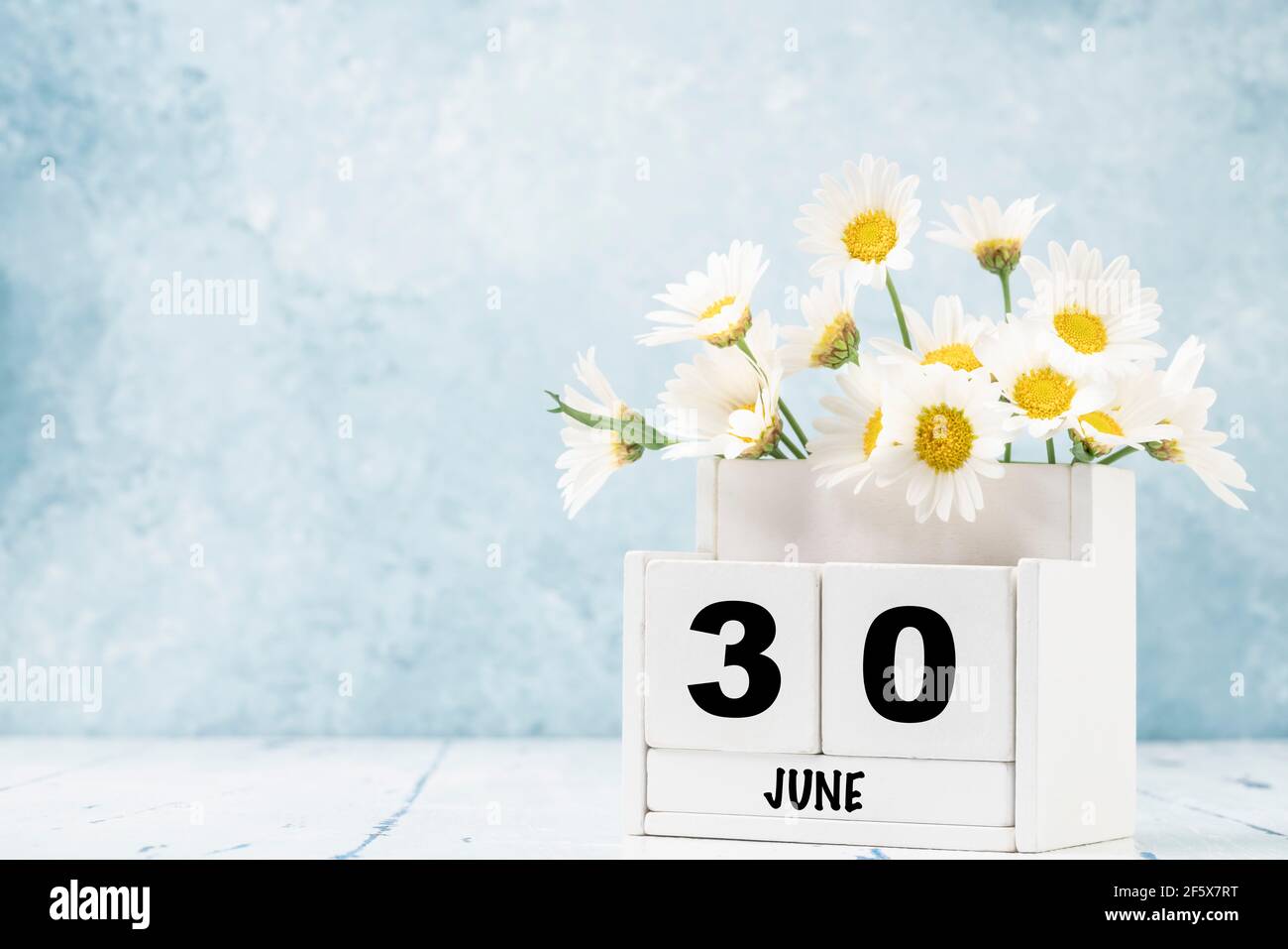 White cube calendar for June decorated with daisy flowers over blue ...