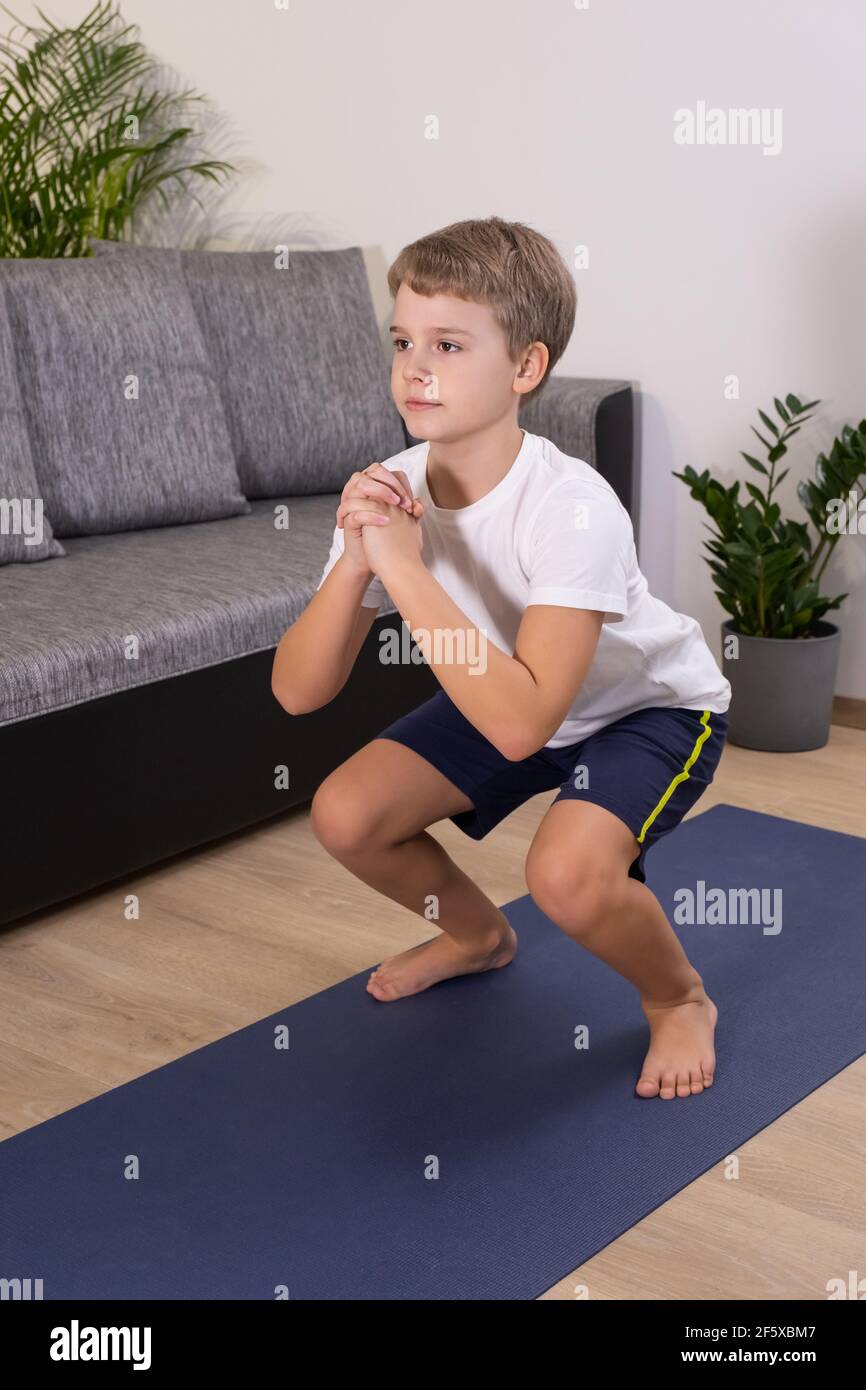 Blond boy goes in for sports on yoga mat. Child physical activity squat ...