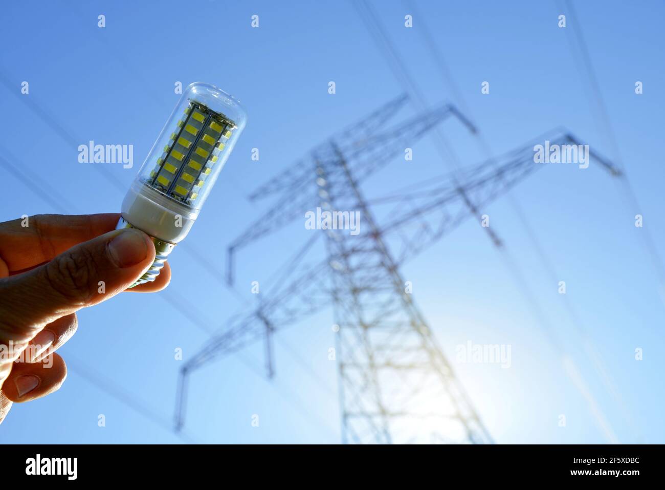 Hand holding eco LED light bulb with transmission tower at the ...
