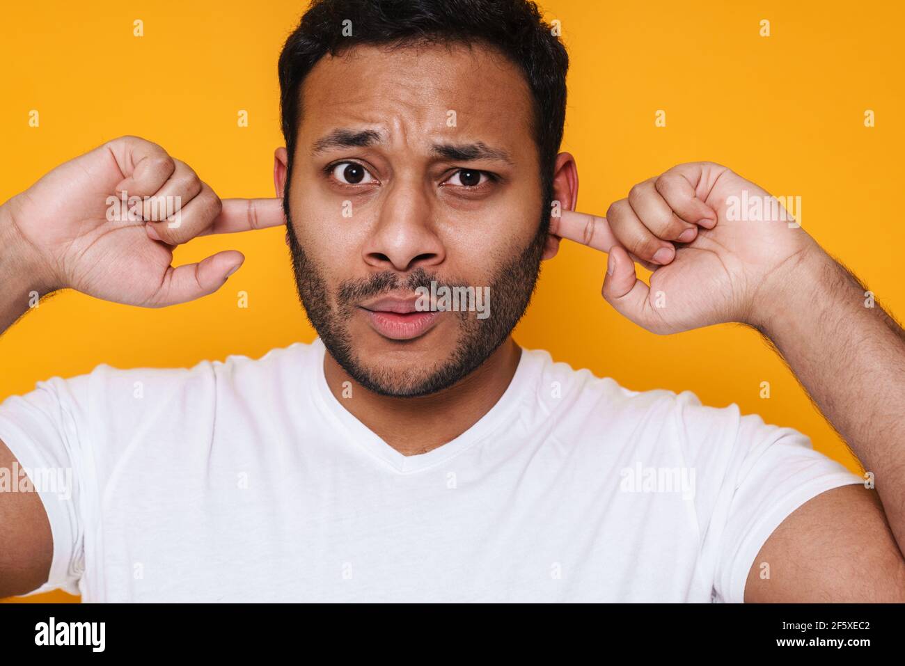 Asian young unshaven man plugging his ears with fingers isolated over ...