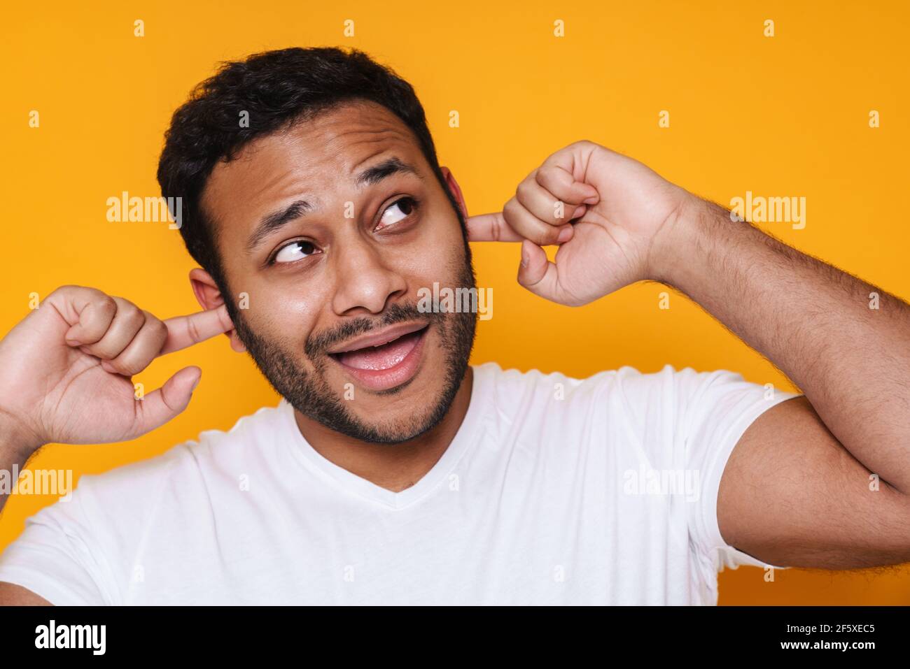 Asian young unshaven man looking upward and plugging his ears with ...