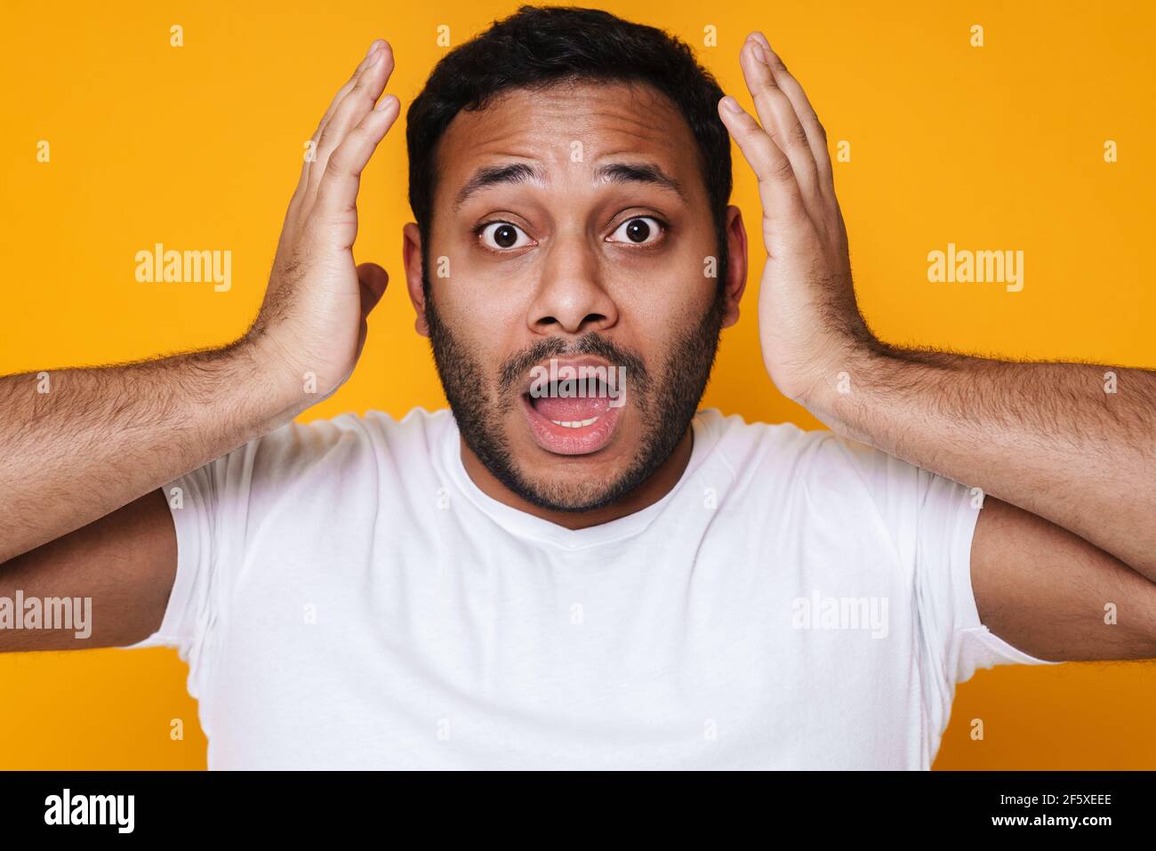 Asian young unshaven scared man grabbing his head isolated over yellow ...