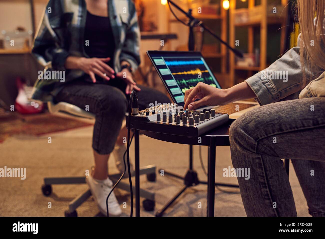 Close-up of two young women sitting in recording studio using laptop ...