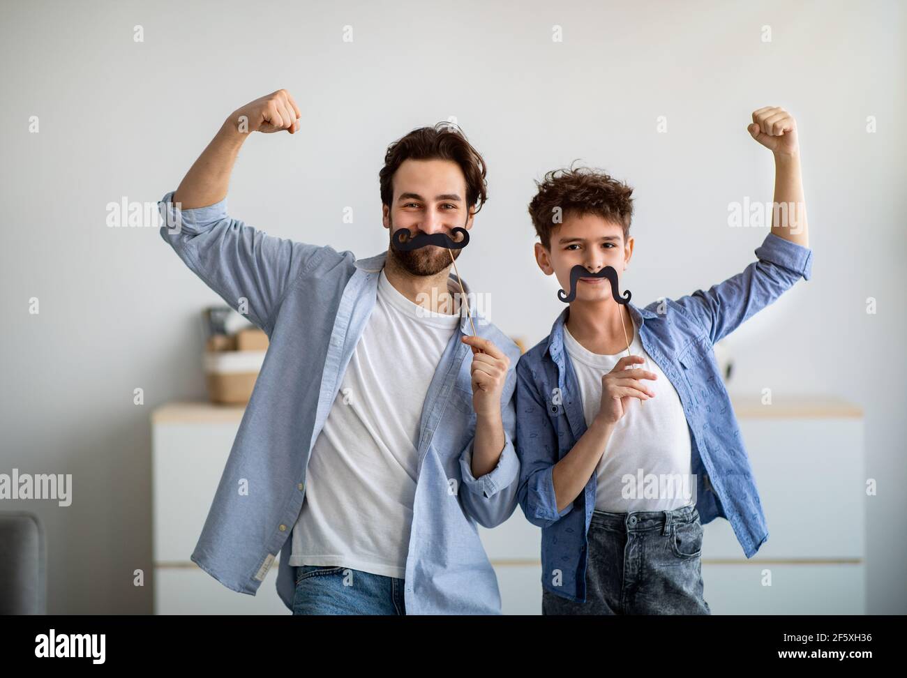 Son and strong dad showing biceps, holding fake moustache on sticks and ...