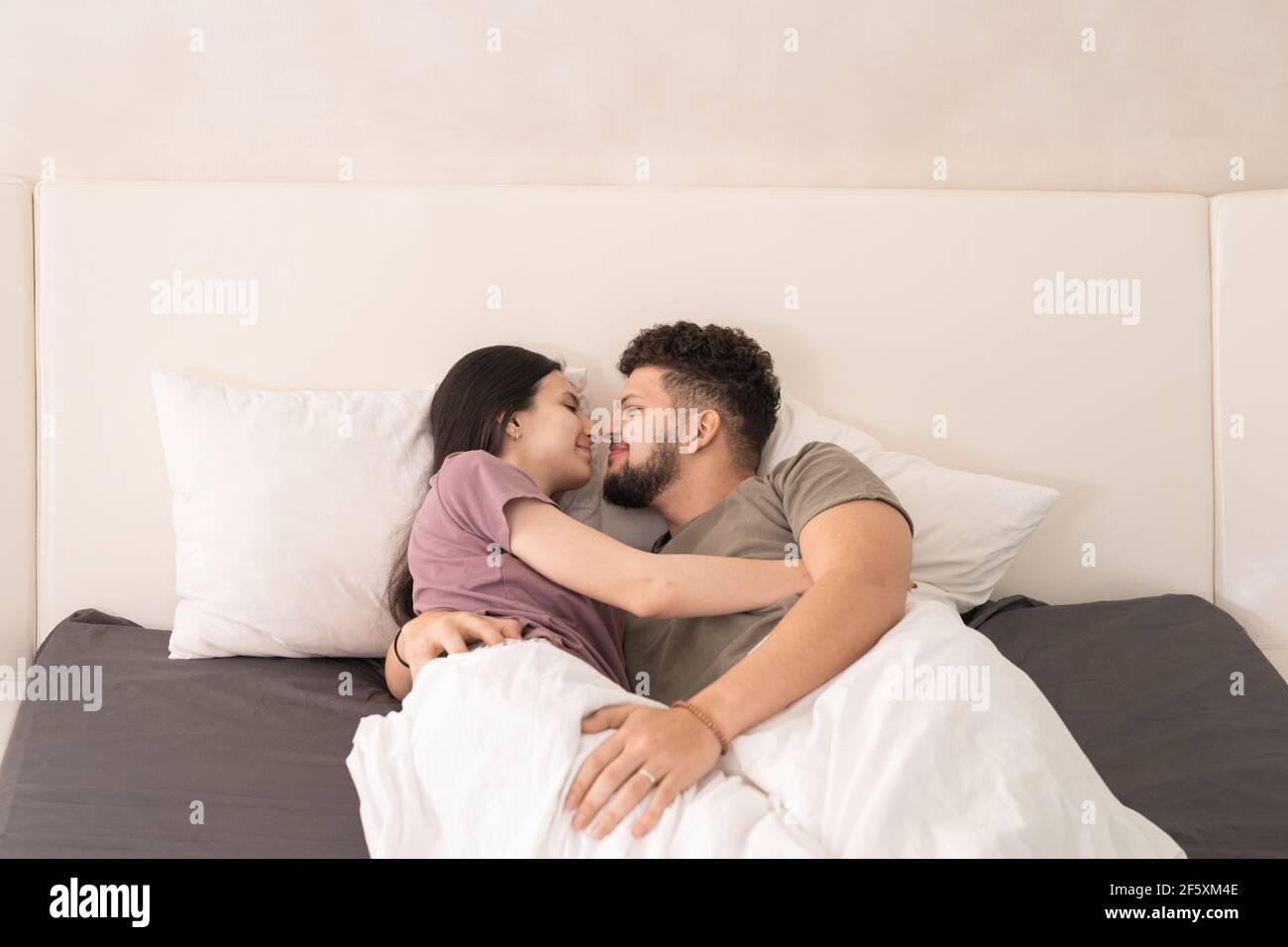Happy young affectionate couple in t-shirts lying in embrace under ...
