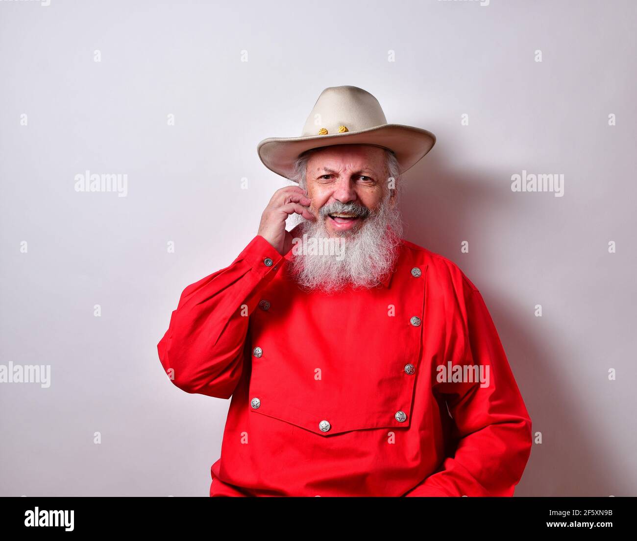 Old rancher in red western bib shirt scratching his long white beard ...