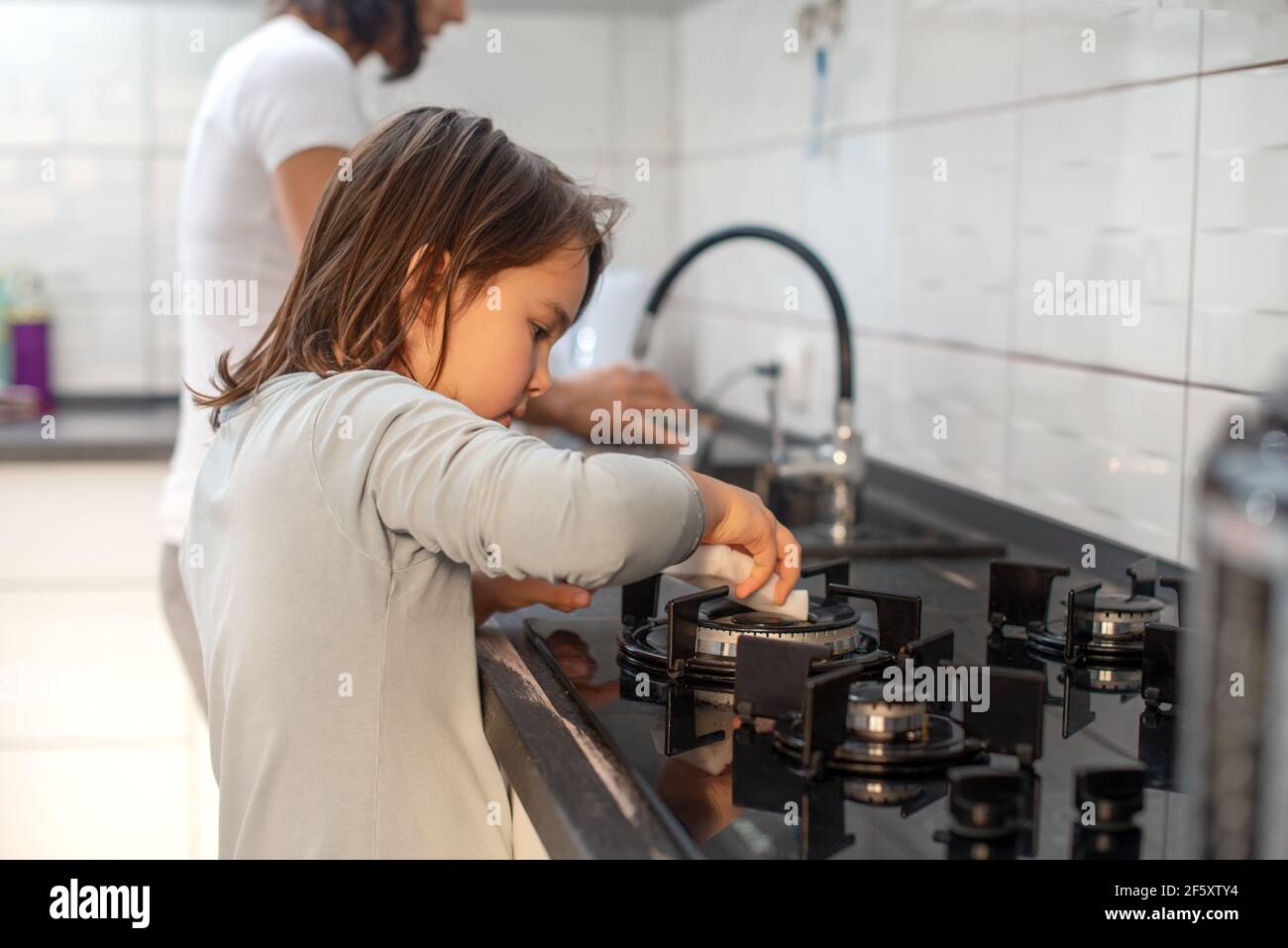 Little girl cleaning dishes in kitchen next to her mother Stock Photo ...