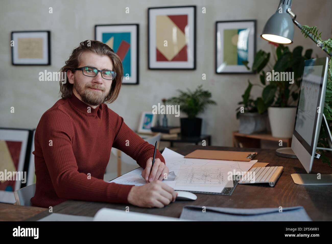 Happy young bearded male architect in eyeglasses and casualwear looking ...