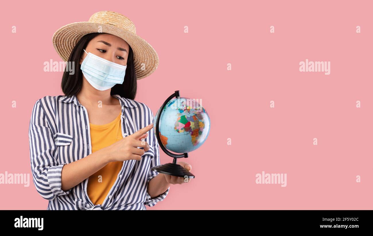 Sad Asian Tourist In Mask Holding Globe, Pointing At Map Stock Photo ...