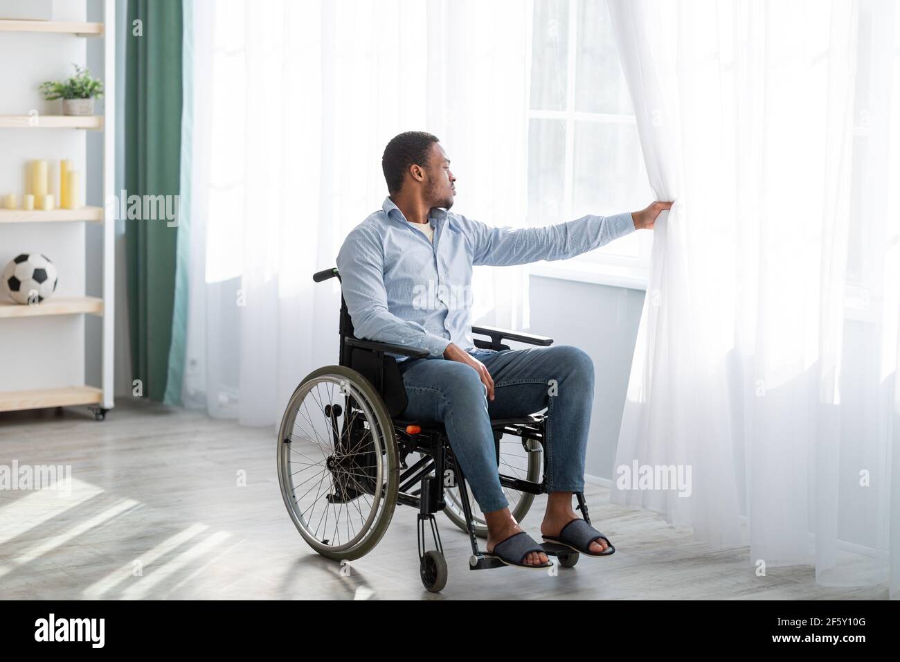 Sad disabled young man sitting on wheelchair alone at home, looking ...