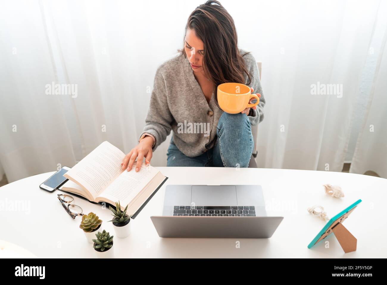 young woman working with computer at home while drinking a cup of coff ...