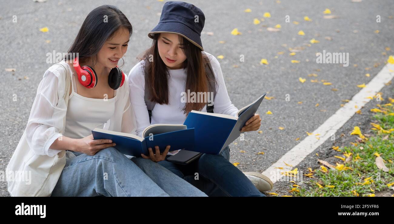 Two happy students sitting and talking each other in a campus at the ...