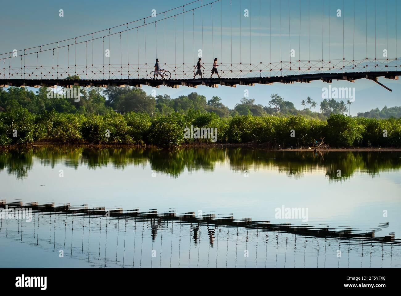 Local hanging bridge in a rural community over a wide river planted ...