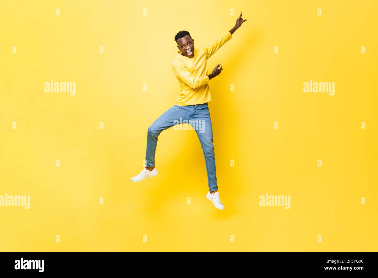 Young cheerful energetic African man jumping and pointing hands up ...