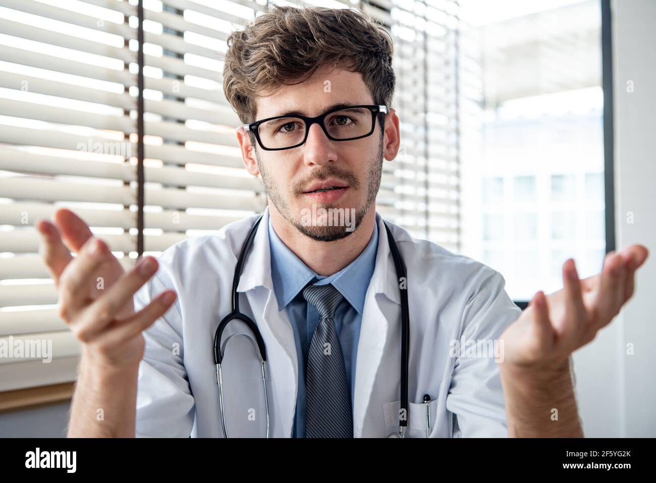 Young male doctor looking at camera explaining and talking with patient ...