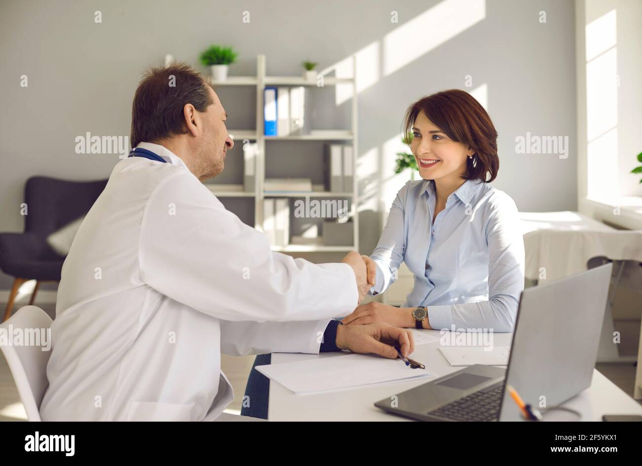 Male doctor greeting handshaking smiling female patient in hospital ...