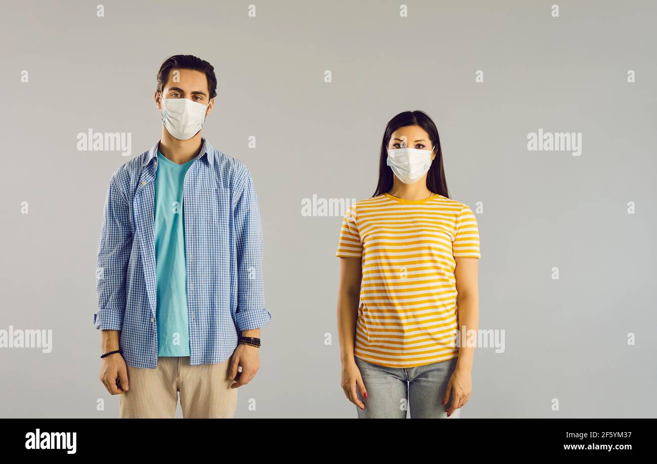 Portrait of two people wearing medical face masks standing on light ...