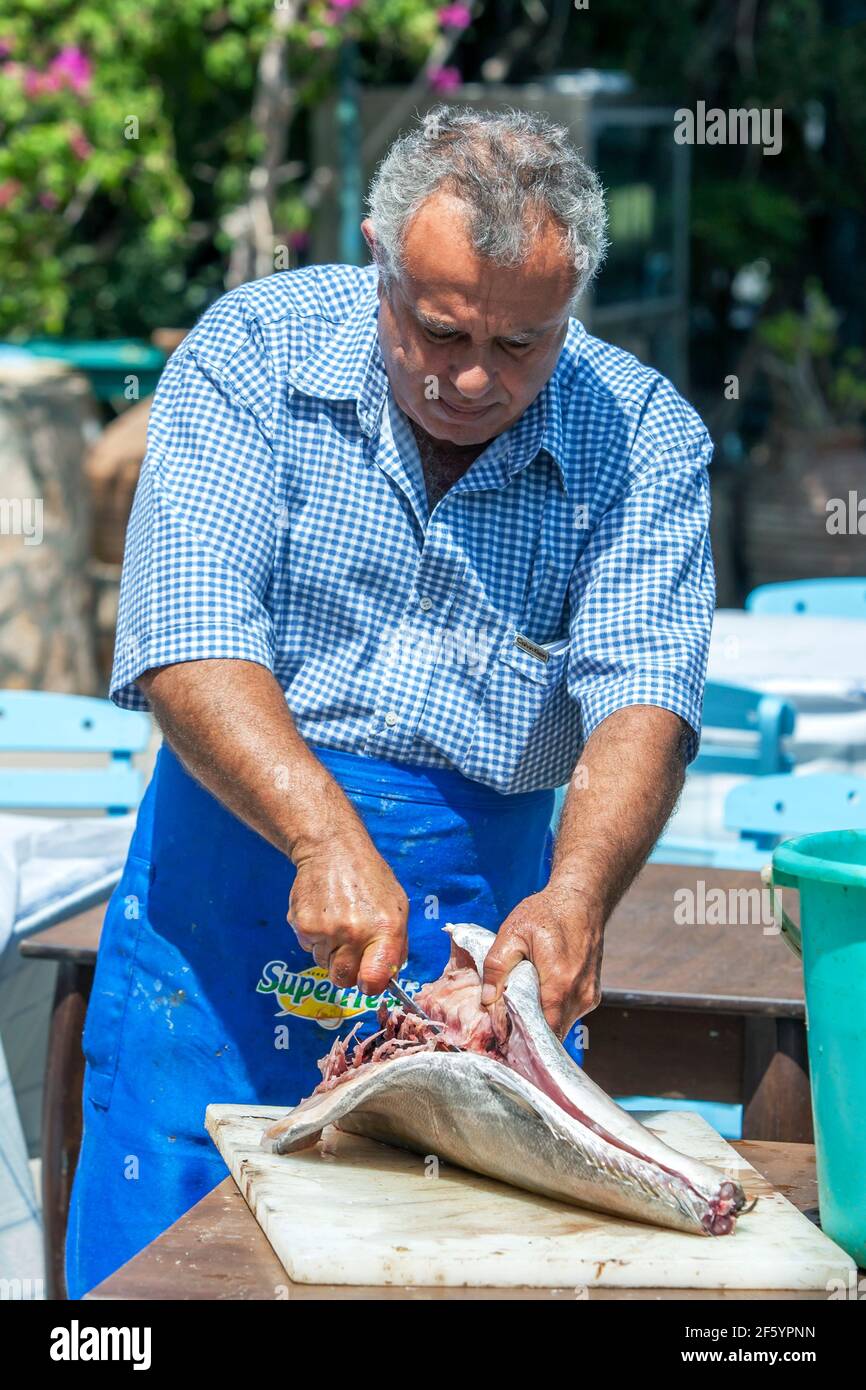 A fishmonger fillets a freshly caught fish at a table adjacent to the ...
