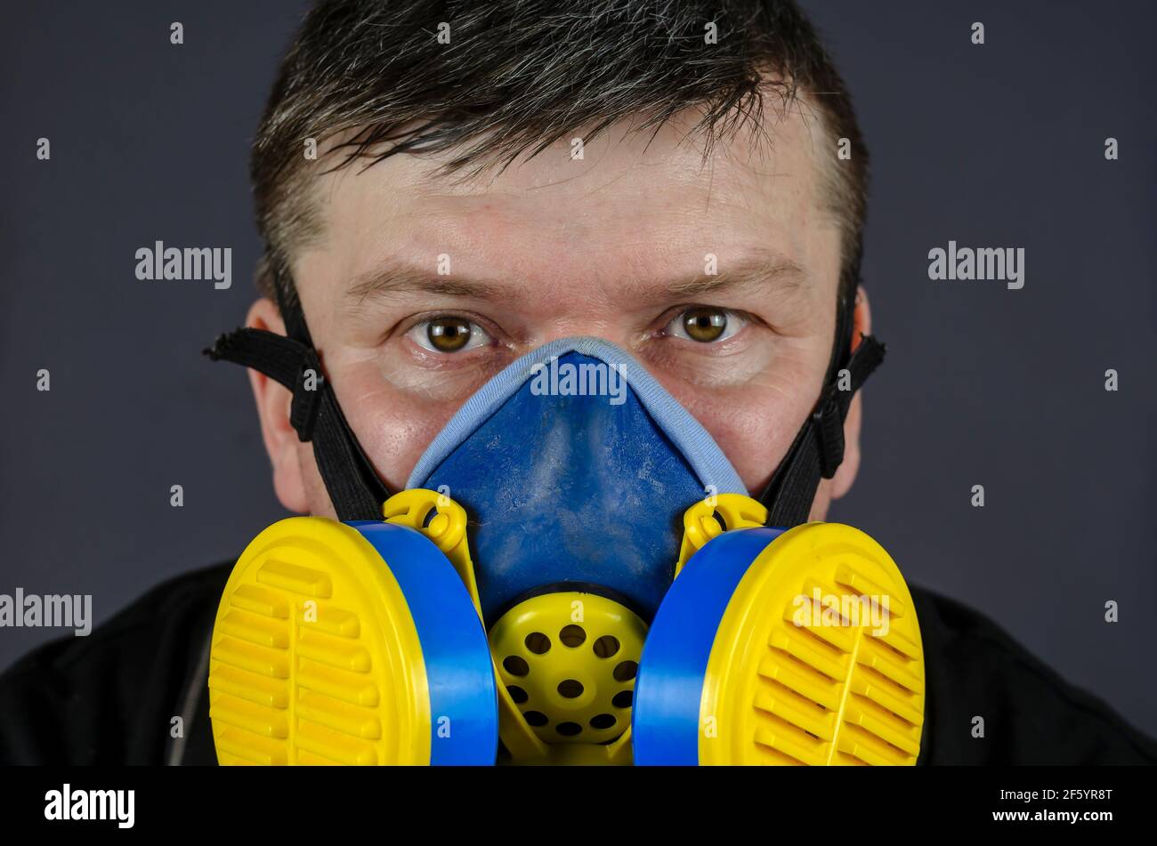 Portrait of a man in an industrial respirator on a gray background. An ...