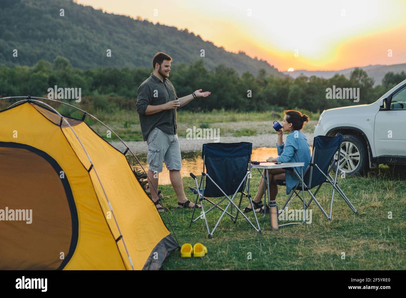 couple sitting in camp chairs looking at sunset above river in ...