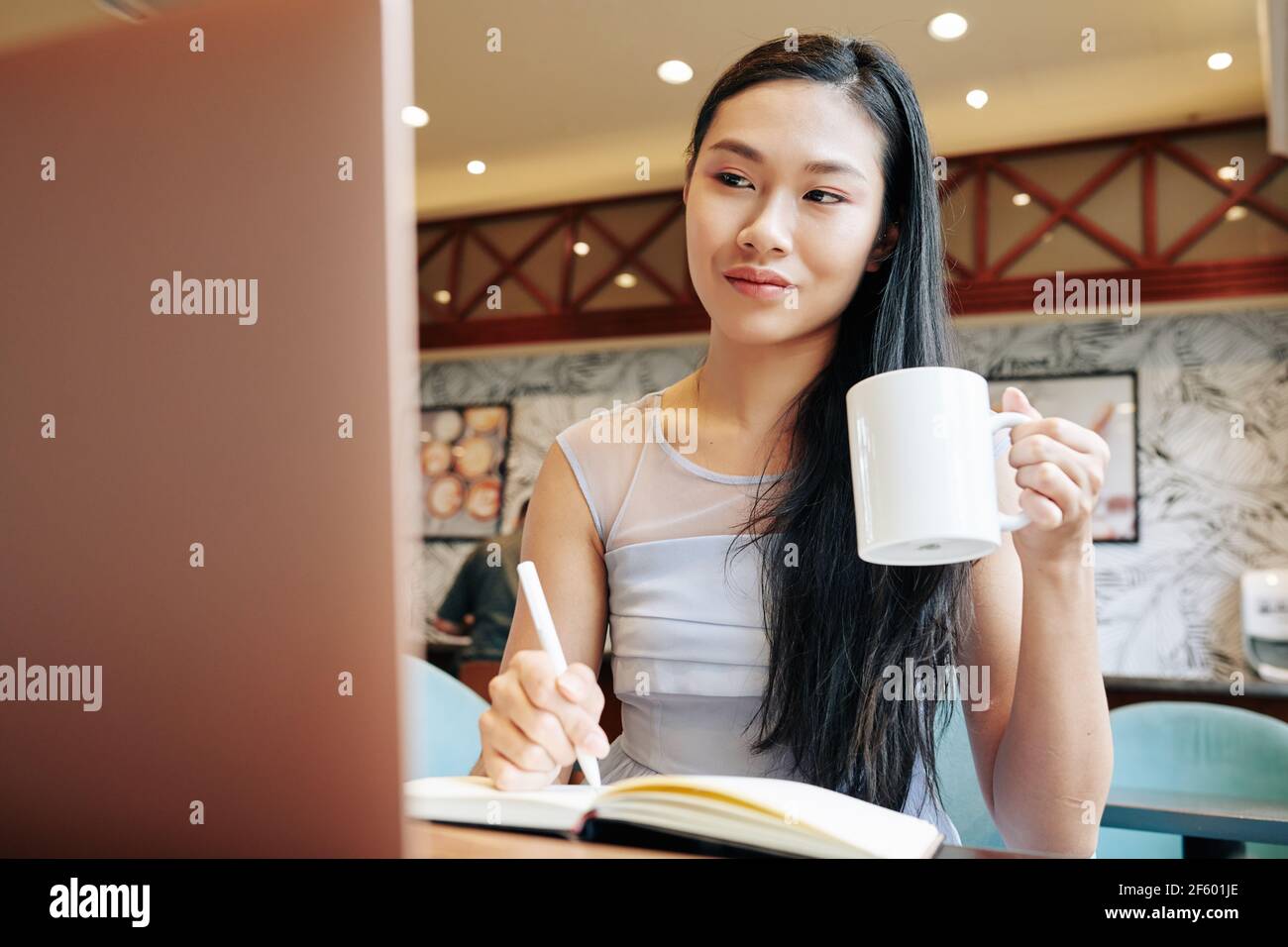 Ppetty young Asian woman drinking morning coffee in cafe, reading news ...