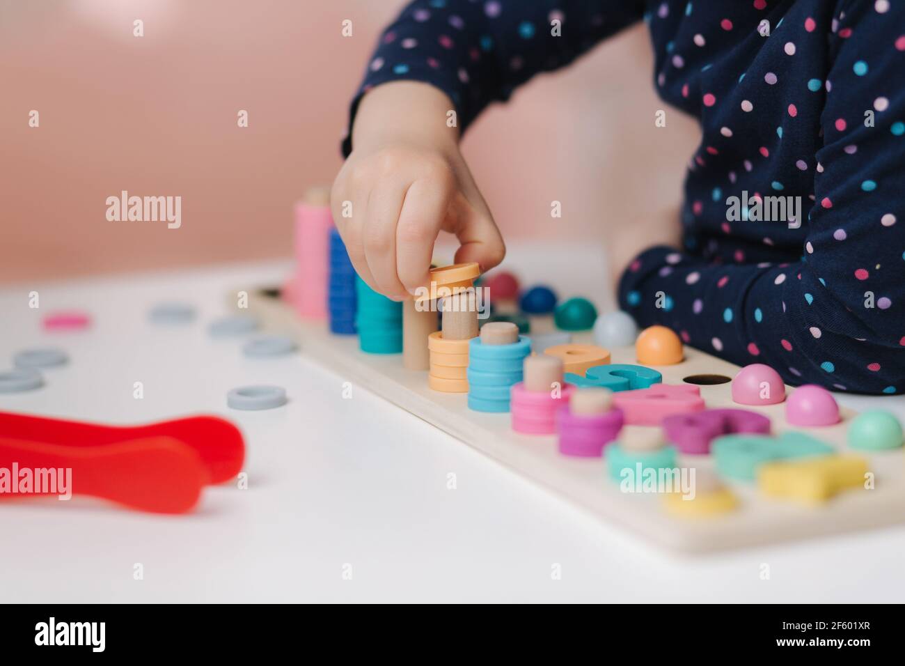 Closeup of kid's hand putting color rings on wooden column. Little girl ...