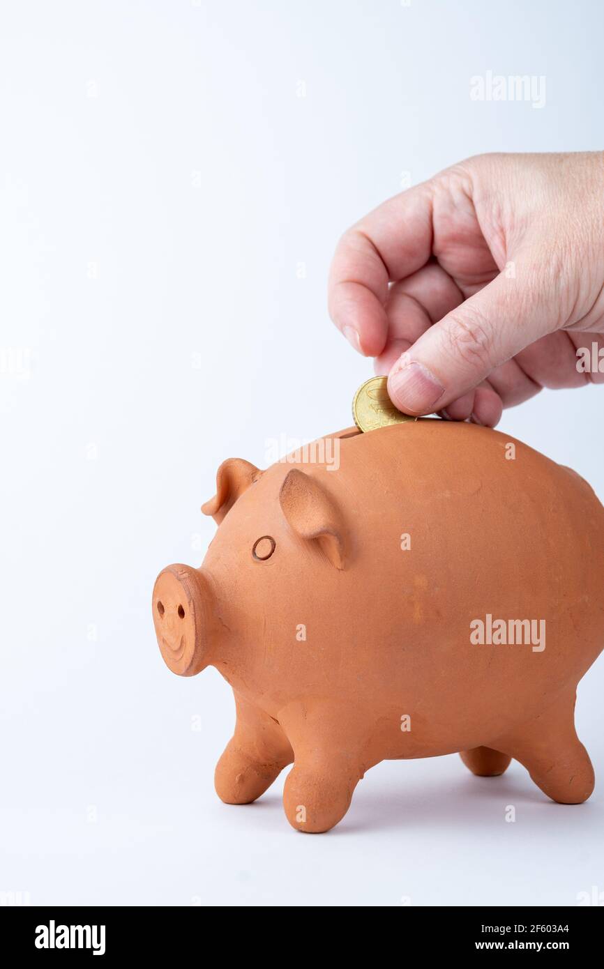 View of hand with coin on piggy bank made of clay, white background ...