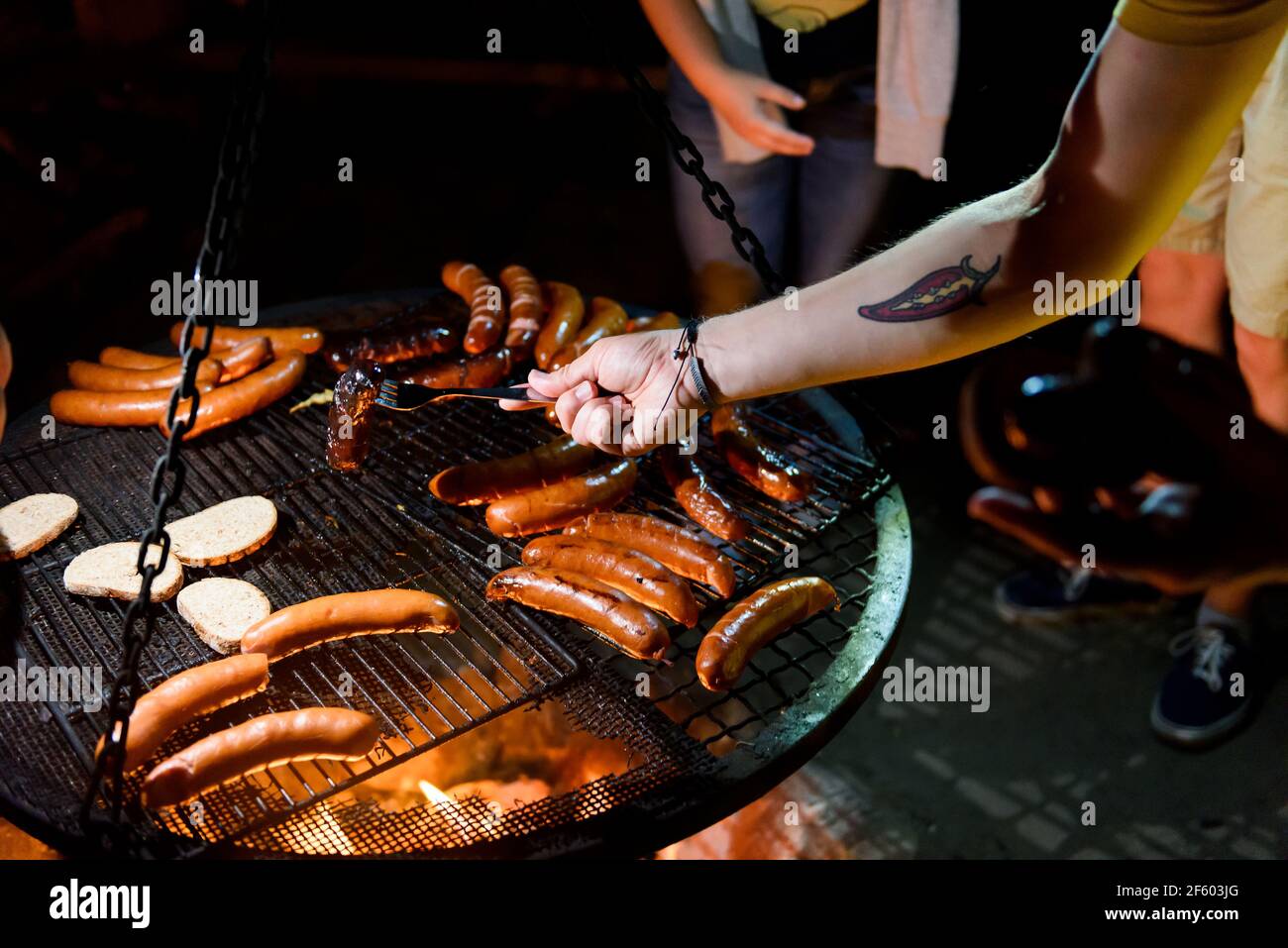 Making barbeque at night. Human hand taking grilled sausage from ...
