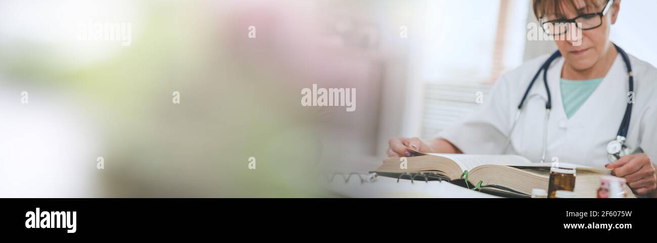 Female doctor reading a textbook in medical office; panoramic banner ...