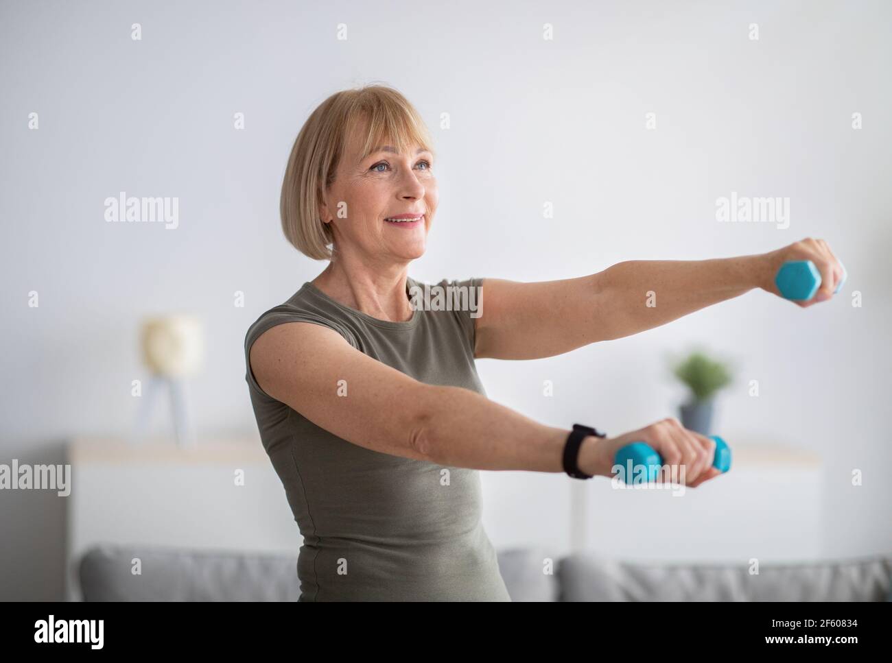 Joyful senior woman doing domestic training, working out with dumbbells ...