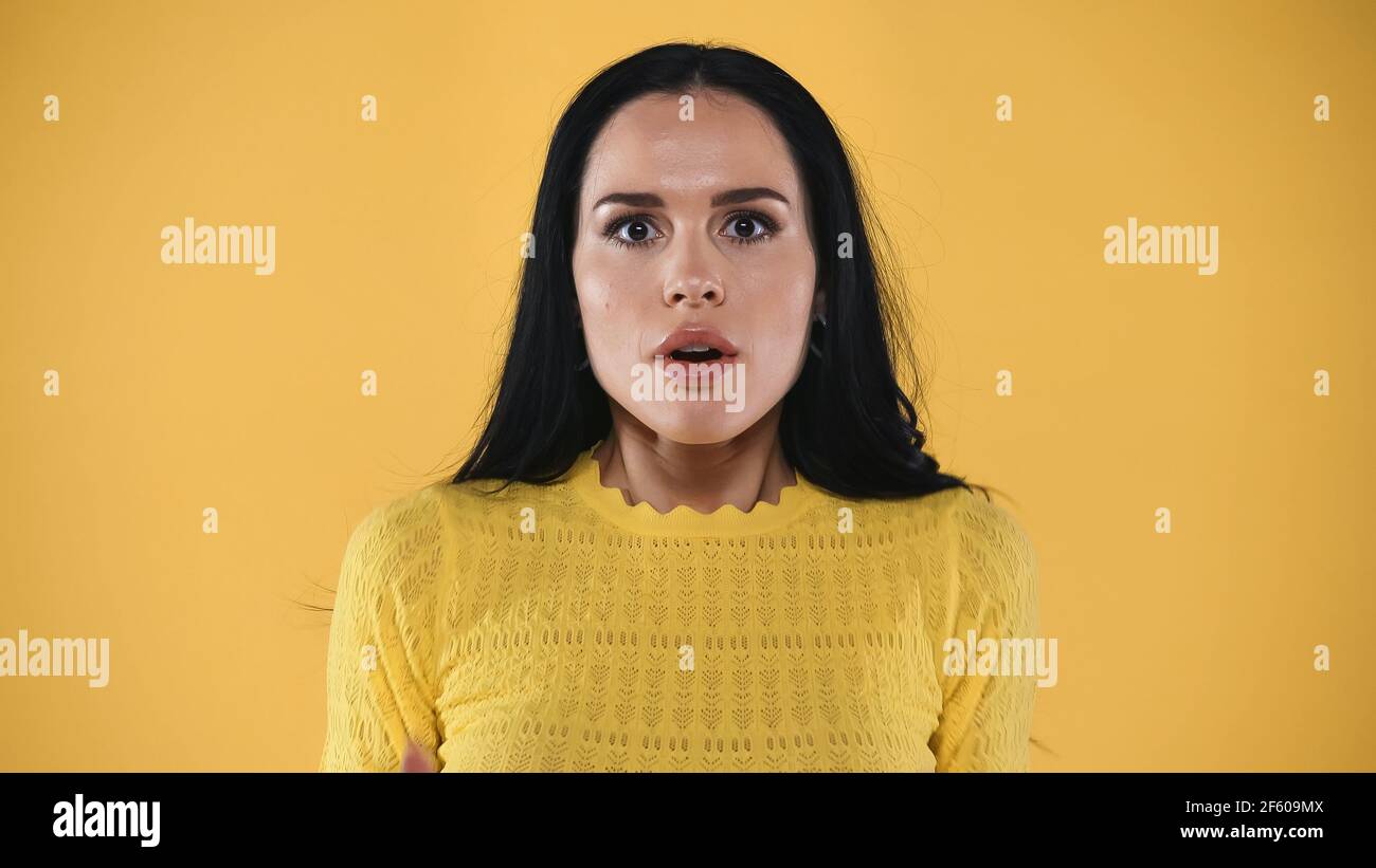 shocked and scared brunette woman looking at camera isolated on yellow ...