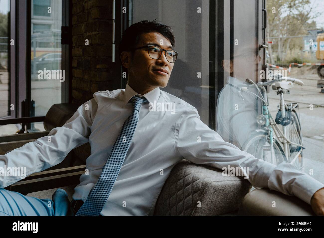 Male entrepreneur looking through window while sitting on sofa at ...
