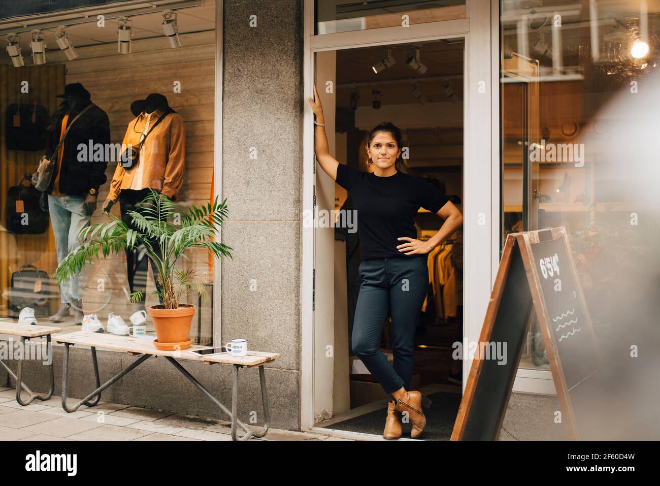Female entrepreneur with hand on hip standing on doorway of retail ...