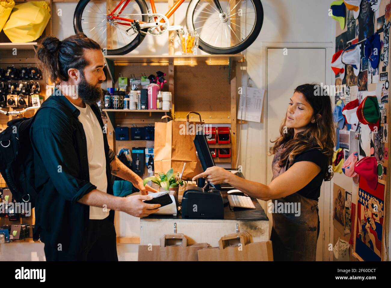 Male customer doing contactless payment to female owner in retail shop ...