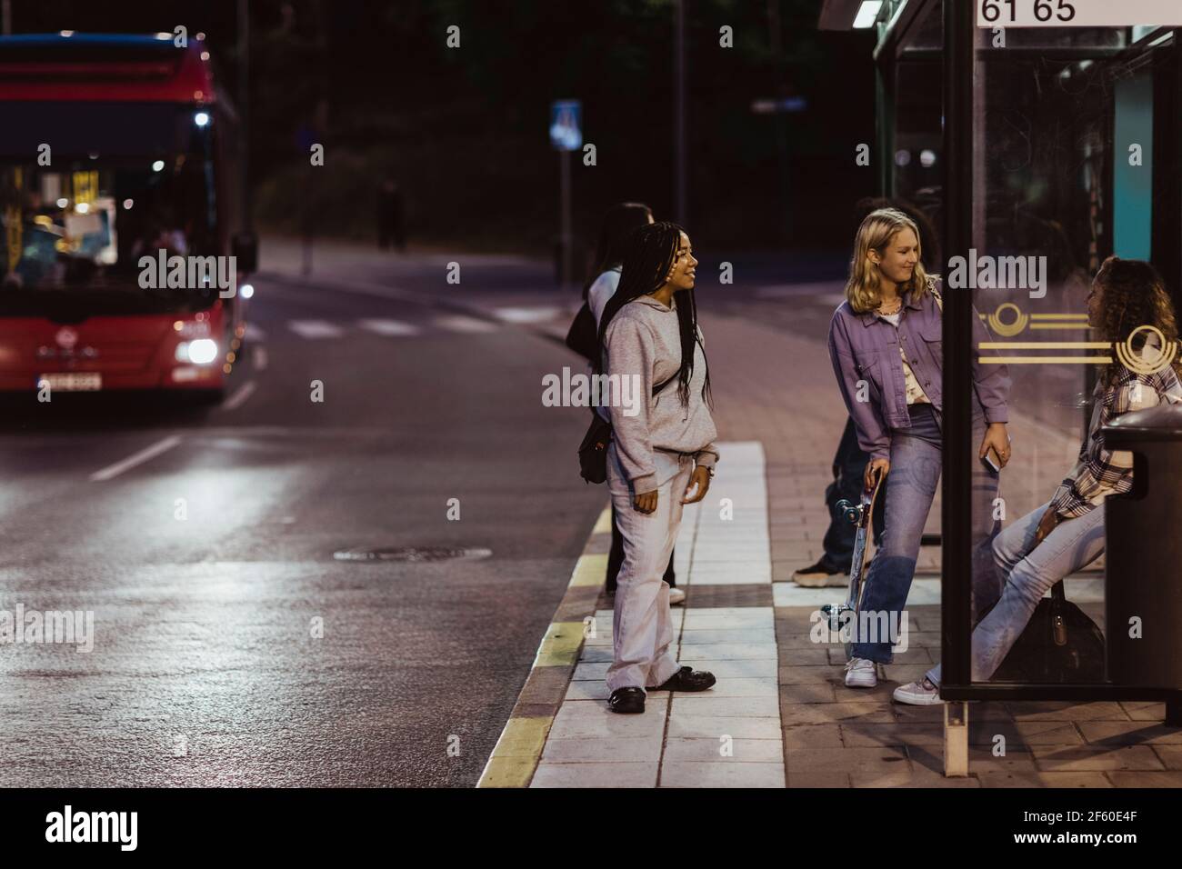 Female friends sitting on bus stop at night Stock Photo - Alamy