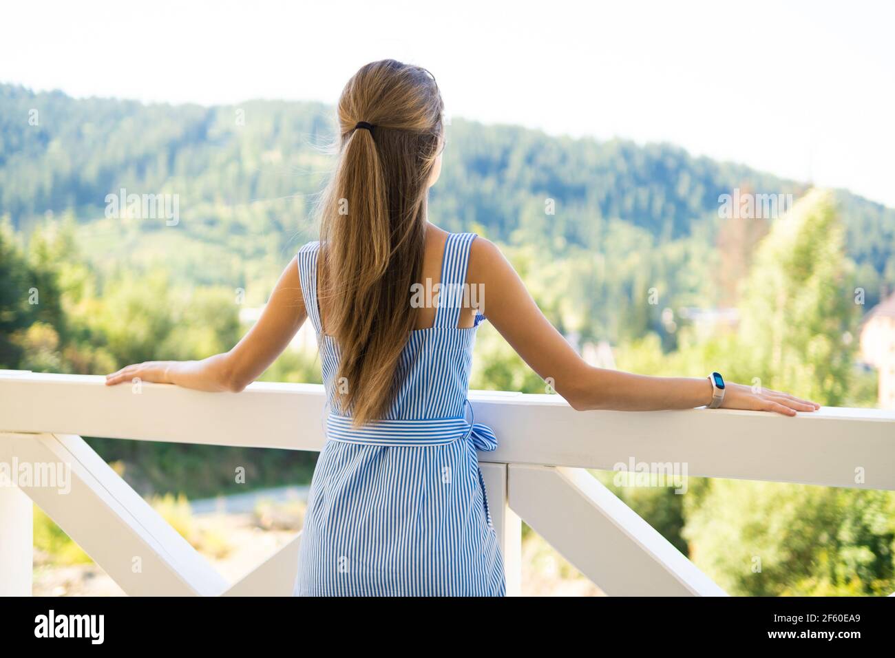 Back view of young beautiful woman at balcony enjoying nature view ...