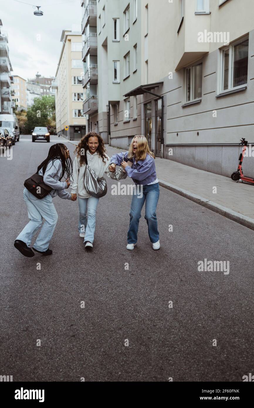 Female friends enjoying while walking on street in city Stock Photo - Alamy