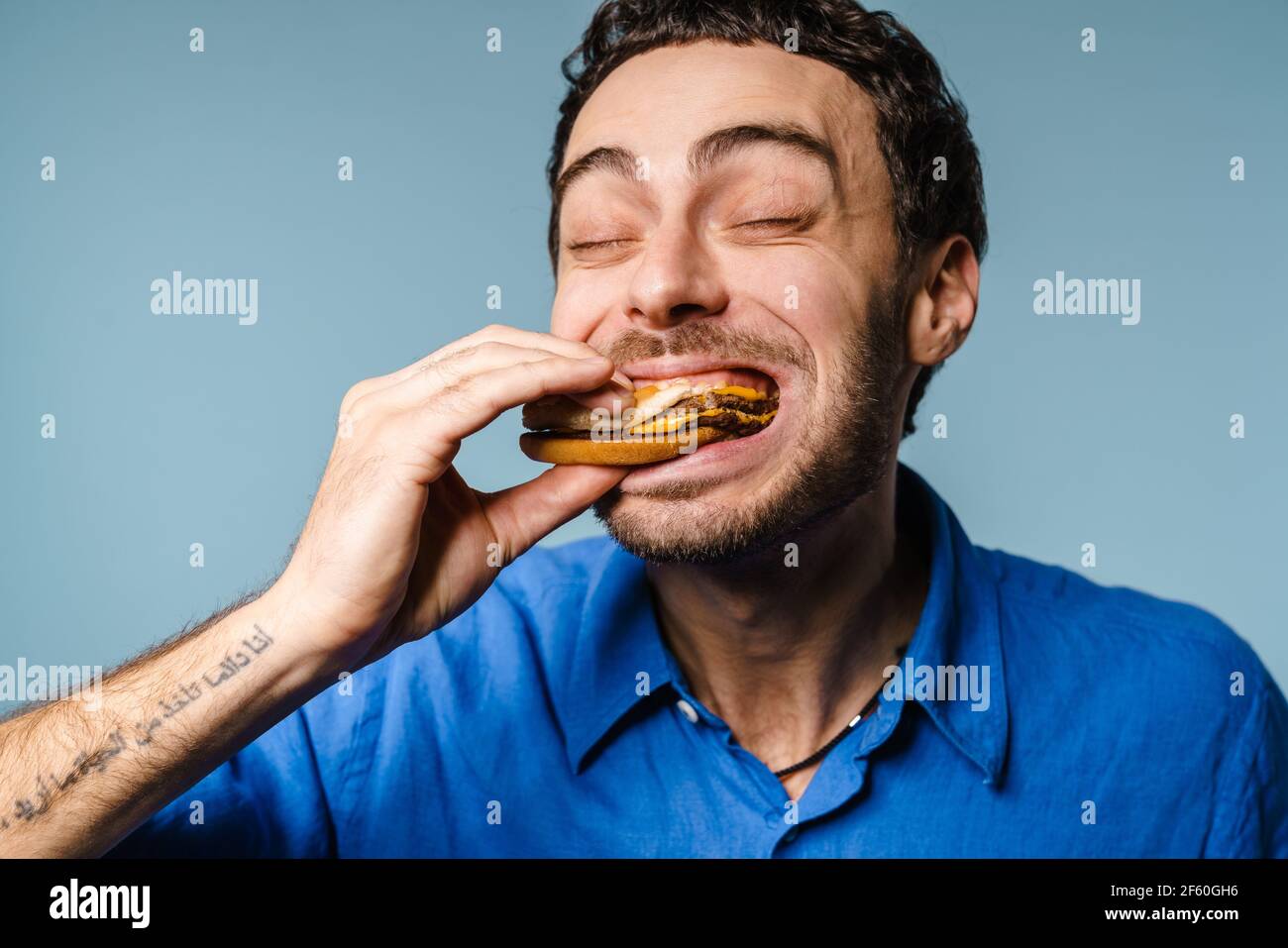 Excited handsome hungry guy eating hamburger on camera isolated over ...