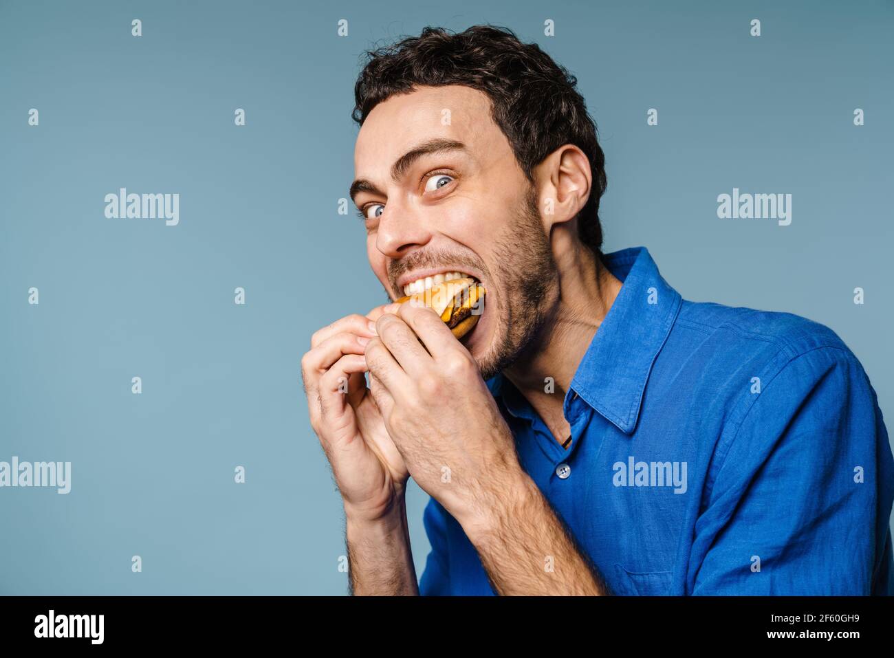 Excited handsome hungry guy eating hamburger on camera isolated over ...