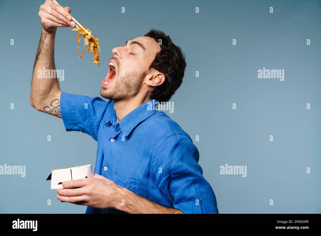 Excited hungry handsome guy eating asian noodles takeaway isolated over ...