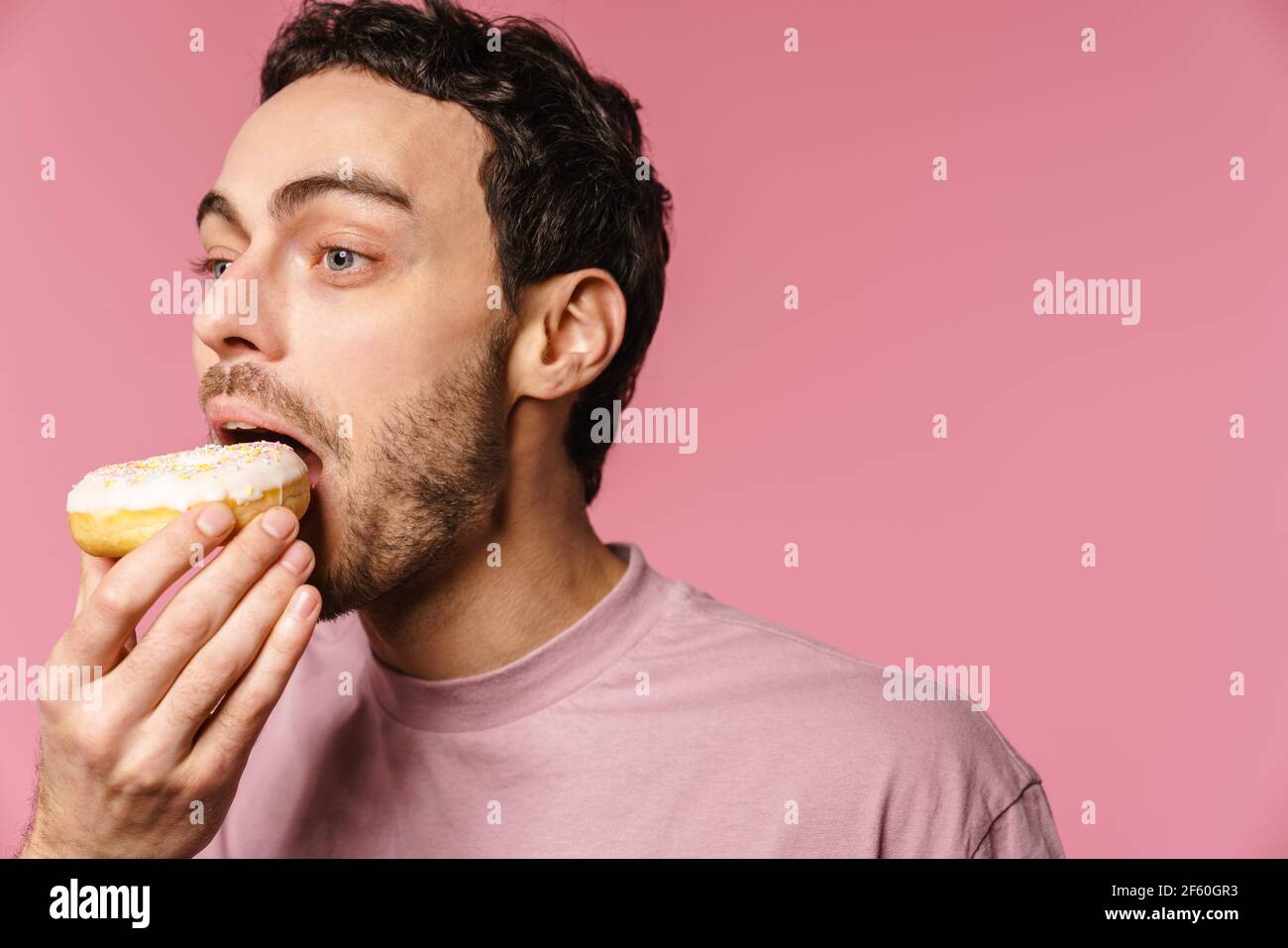 Pleased handsome hungry guy eating doughnut on camera isolated over ...