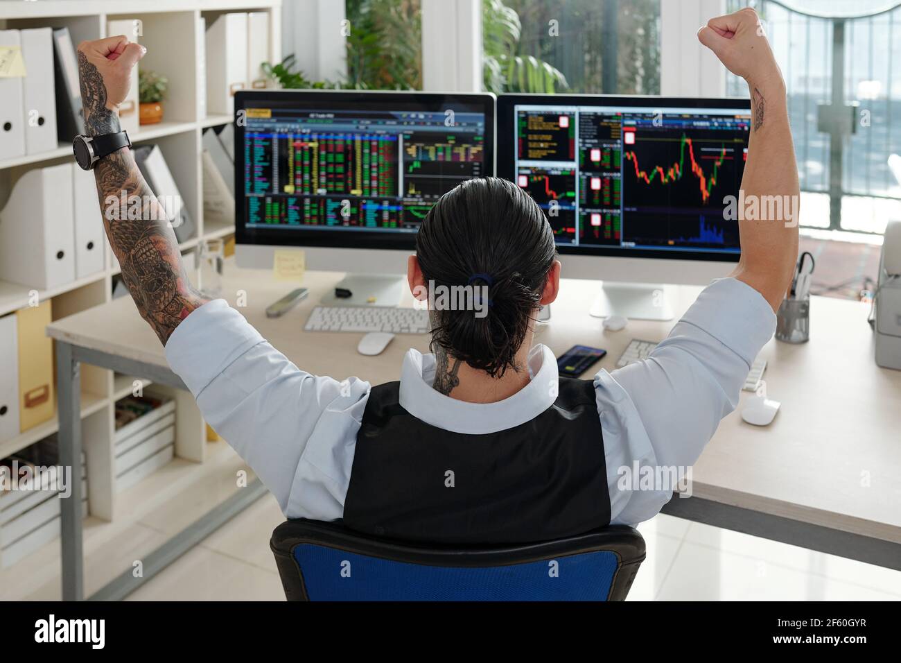 Excited male trader with ponytail raising hands when celebrating ...