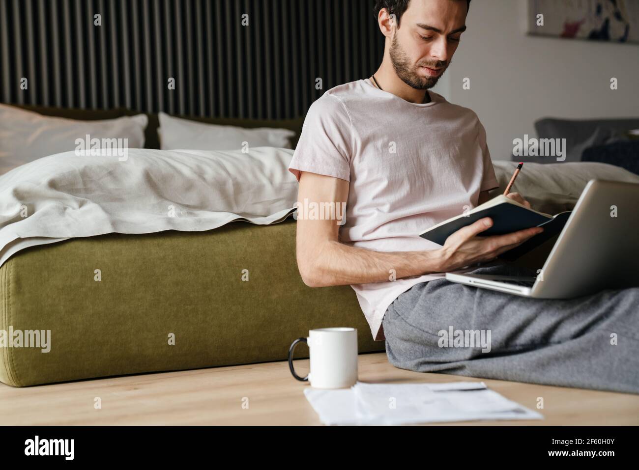 Handsome focused man writing down notes while working with laptop on ...
