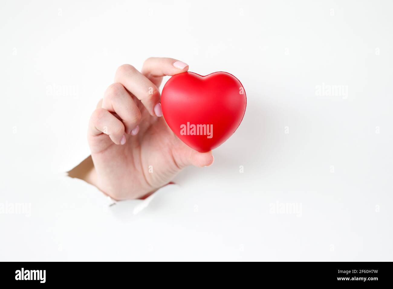 Hand pulling out toy red heart from torn paper Stock Photo - Alamy