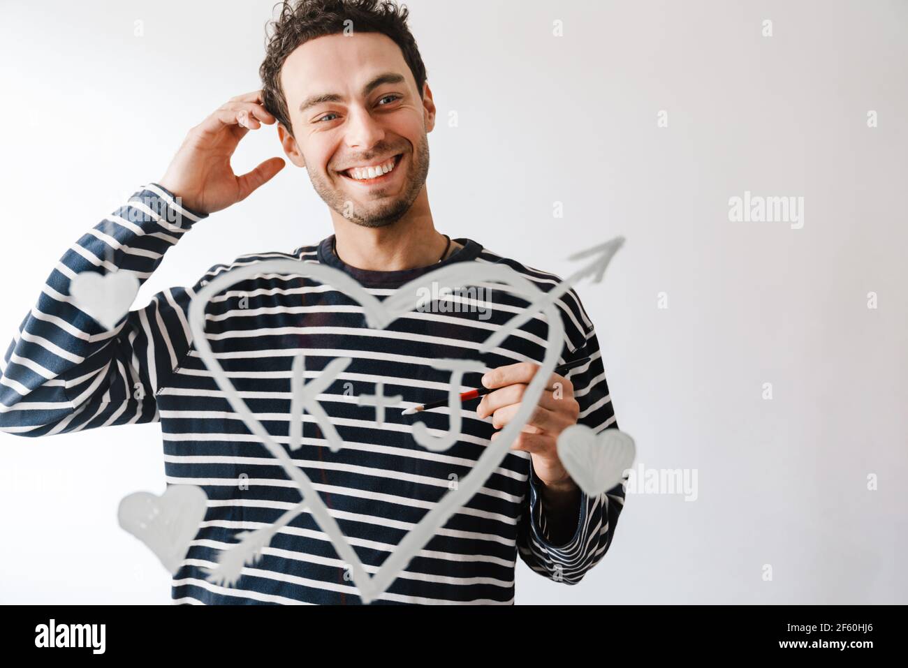 Smiling handsome young man in love drawing a heart symbol isolated over ...