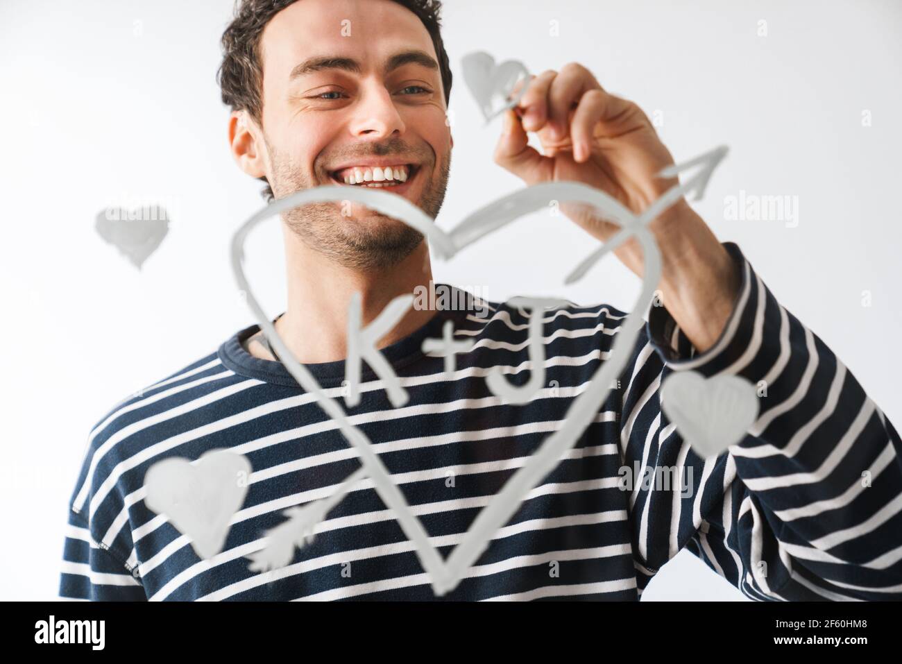 Smiling handsome young man in love drawing a heart symbol isolated over ...