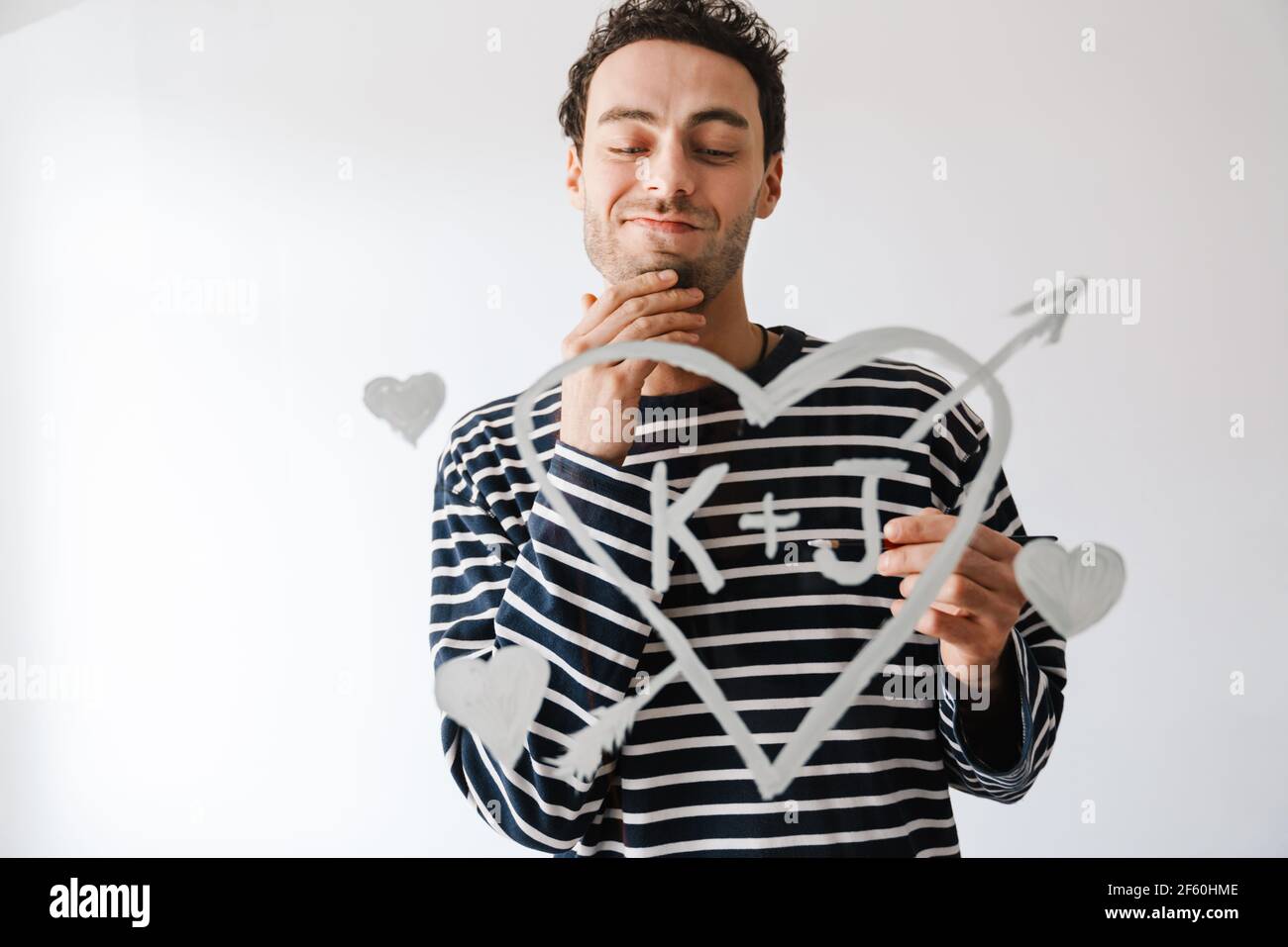 Smiling handsome young man in love drawing a heart symbol isolated over ...