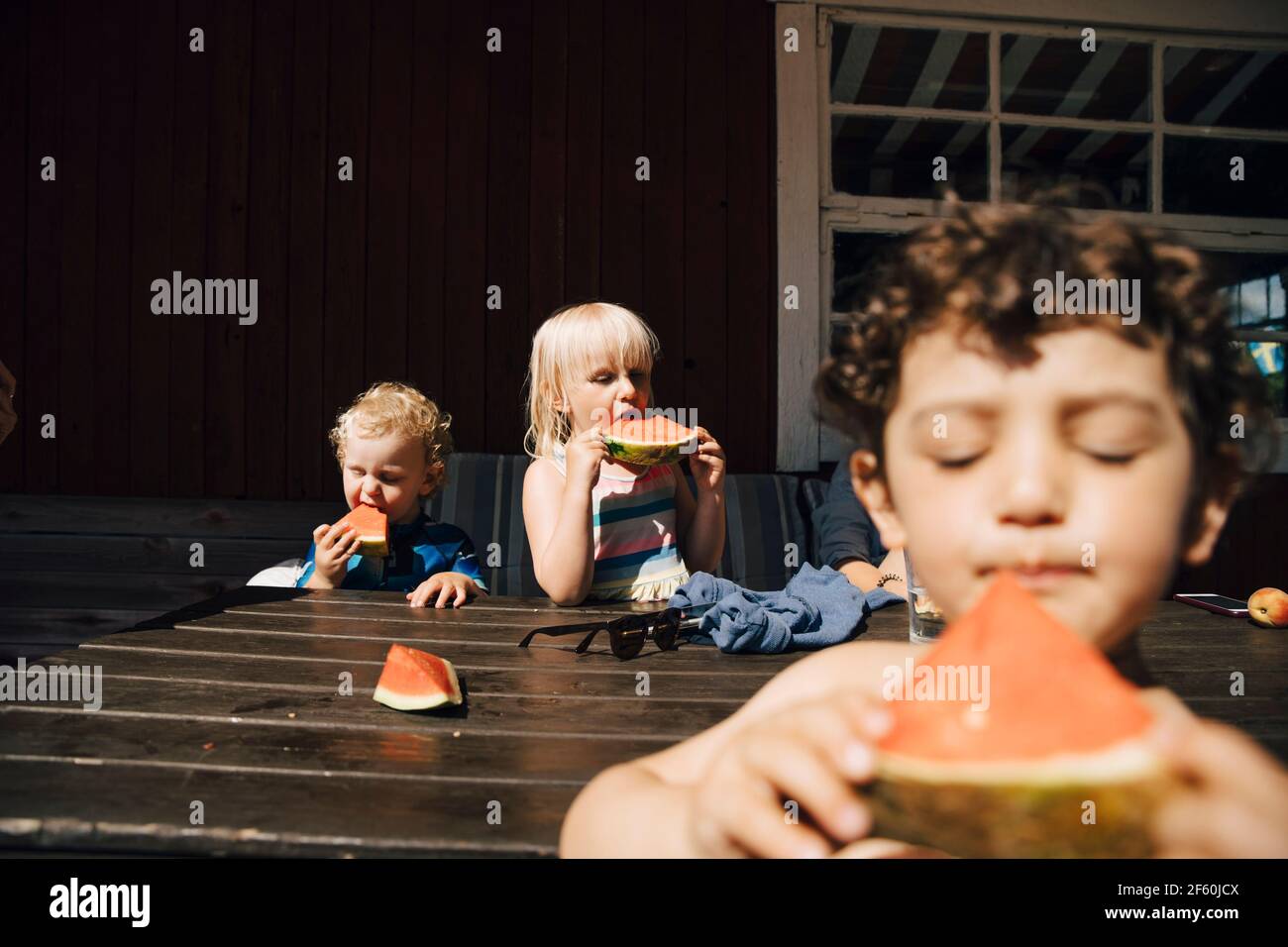 Siblings eating fruit while standing by table during sunny day Stock ...